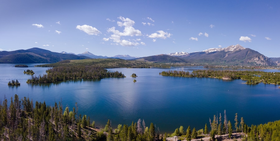 Um lago extenso rodeado por florestas densas e montanhas com picos nevados.