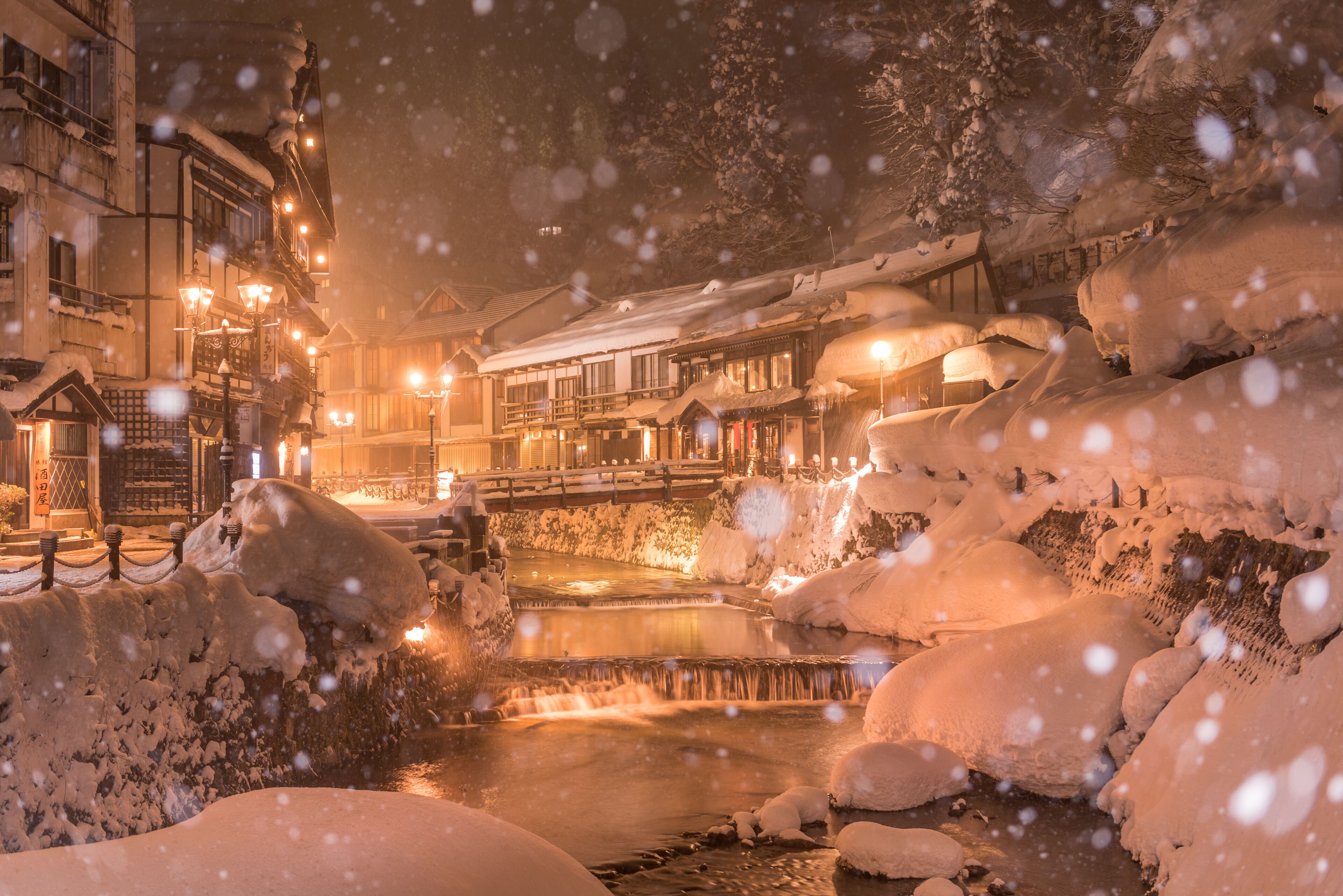 Vila coberta de neve com edifícios iluminados e um riacho congelado.