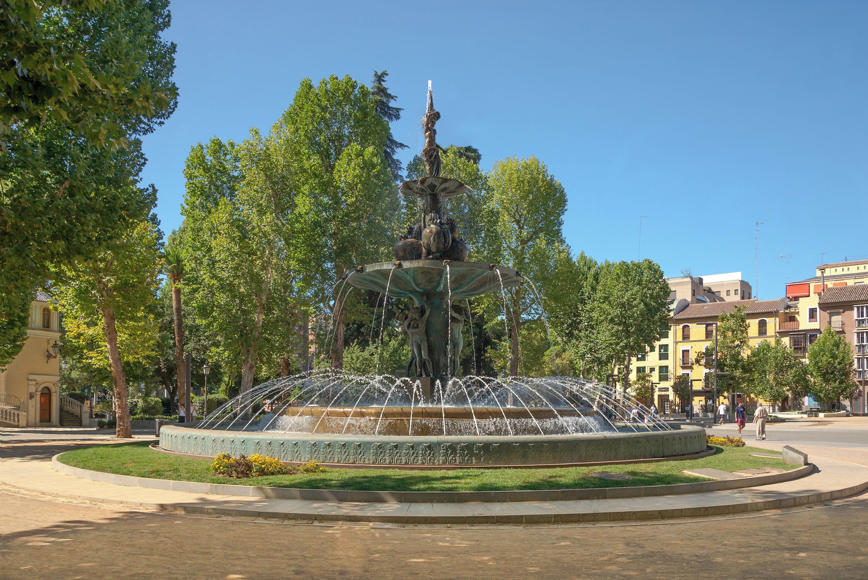 Uma fonte com uma estátua no centro, rodeada por árvores e edifícios.