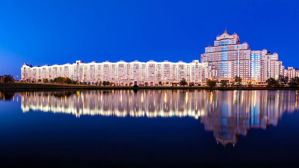 Paisagem urbana à beira-mar, com um grande hotel e outros edifícios refletidos em águas calmas.