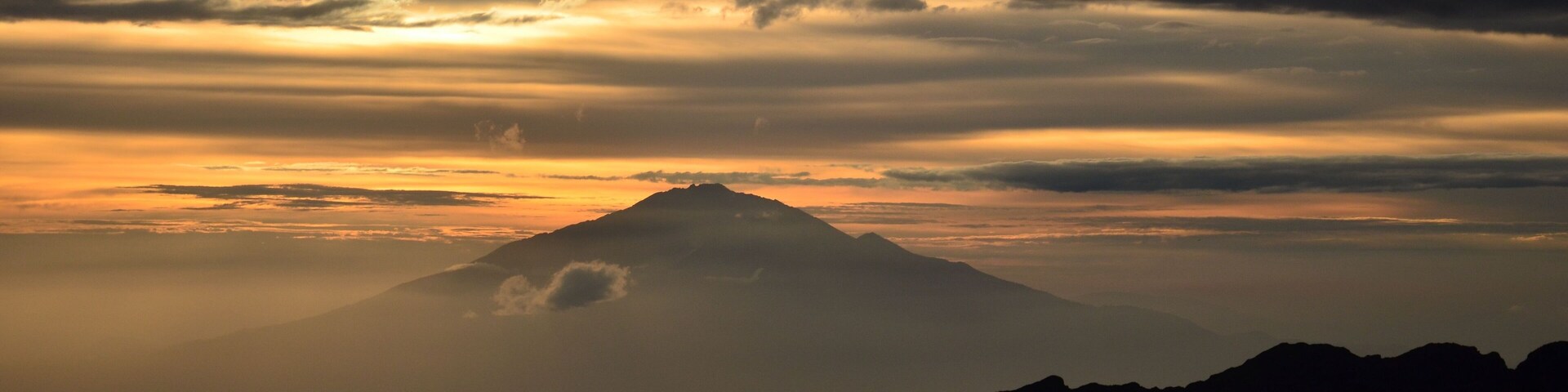 Silhueta de montanha com céu nublado ao pôr do sol.