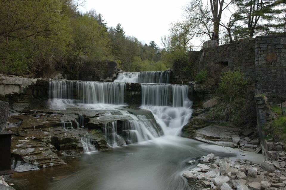 Uma cascata com vários níveis, rodeada por terreno rochoso e árvores.