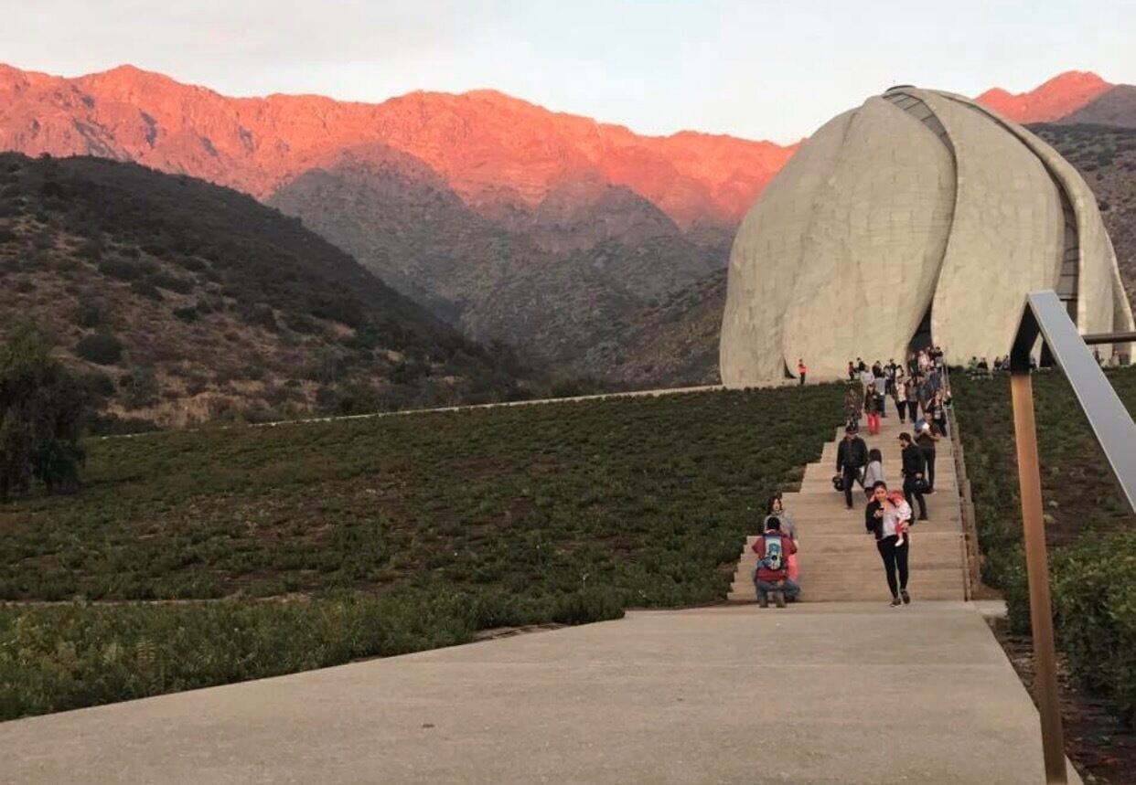 Um edifício grande em formato de cúpula com uma escadaria que leva até ele, situado em meio a uma paisagem montanhosa.