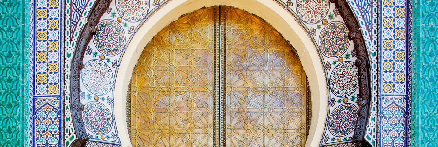 Uma arcada ricamente decorada com azulejos elaborados e uma grande porta de madeira.
