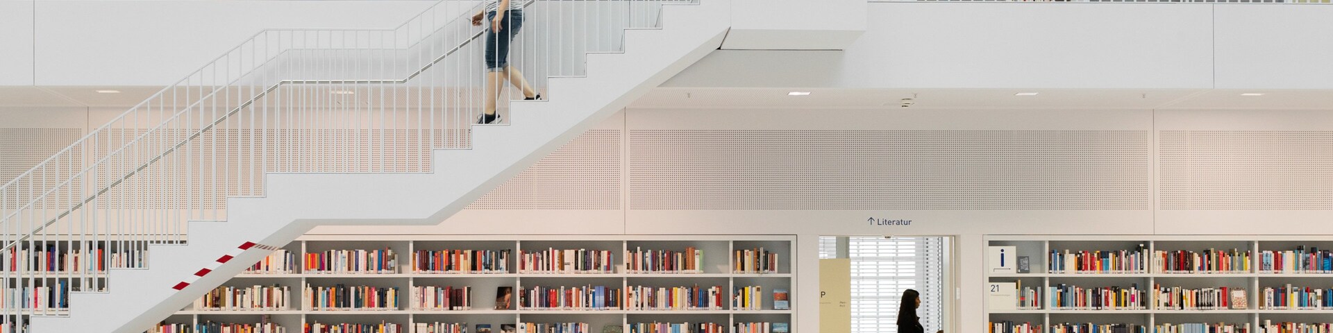 Uma biblioteca moderna com vários andares, corrimãos brancos e vastas coleções de livros.