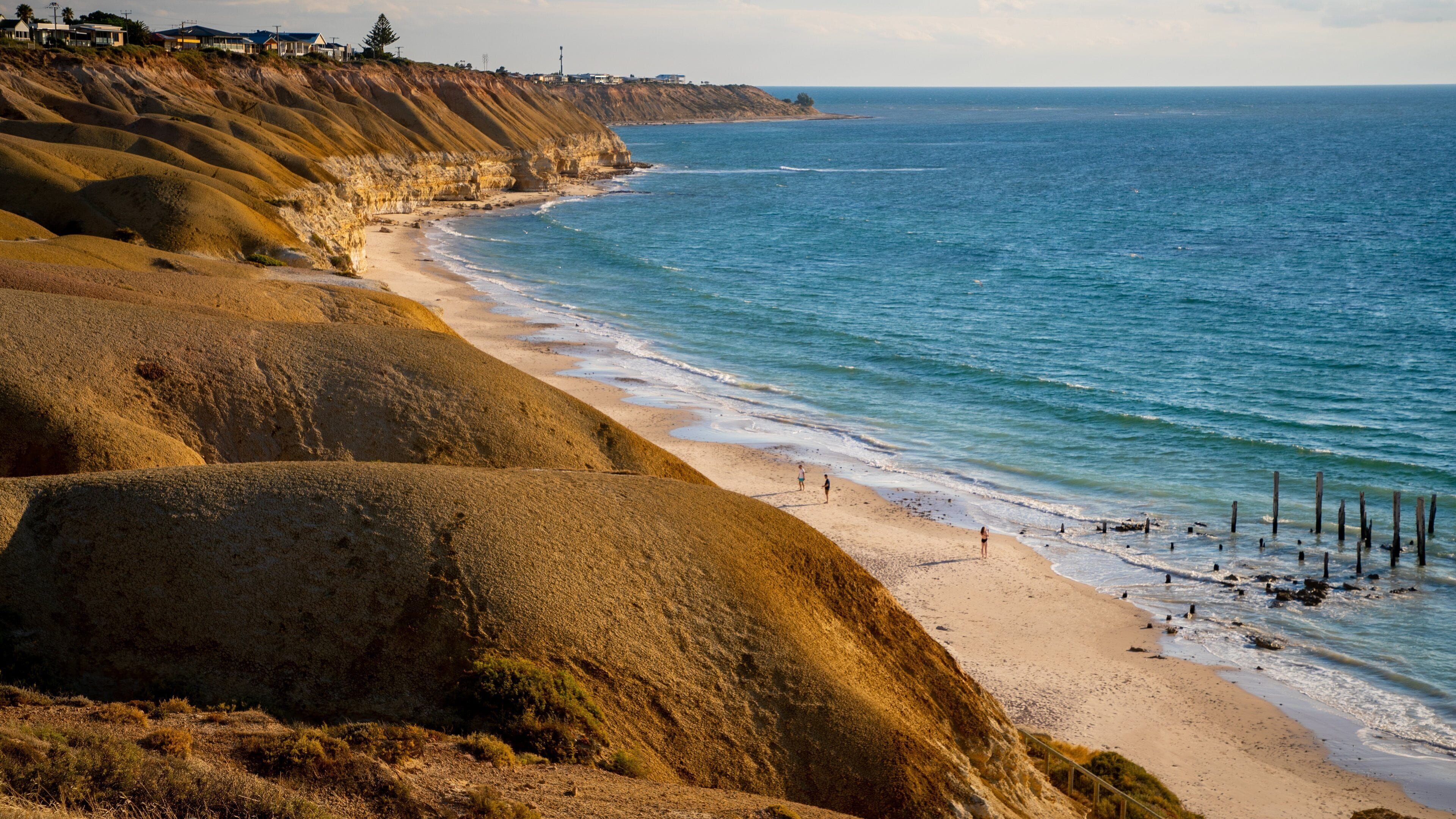 Paisagem costeira com uma praia arenosa, colinas ondulantes e oceano azul límpido.