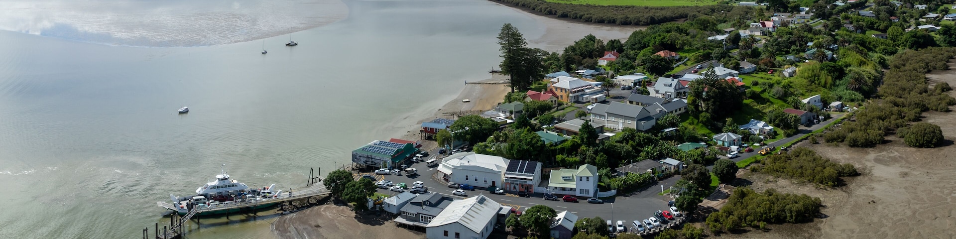 Uma vila costeira com marina, praia de areia e vegetação exuberante.