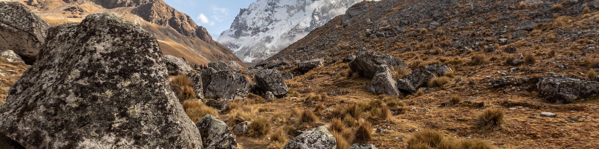 Paisagem montanhosa com terreno rochoso, pouca grama e céu claro.