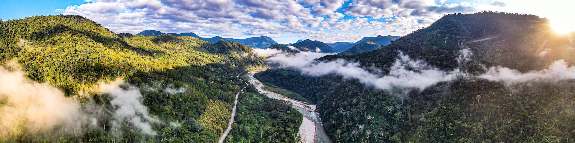 Um rio serpenteia por uma paisagem montanhosa com florestas densas e uma estrada que o acompanha.