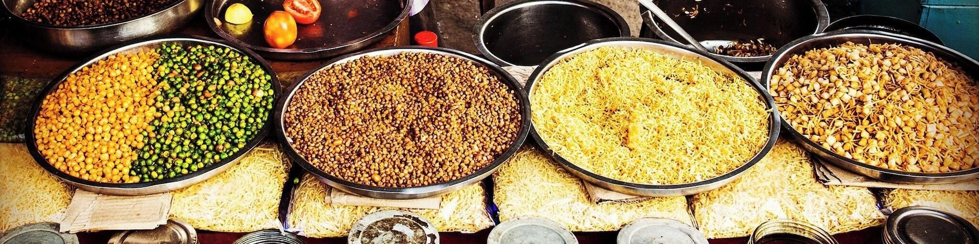 Diversos alimentos expostos em tigelas e potes de metal em uma banca de mercado.