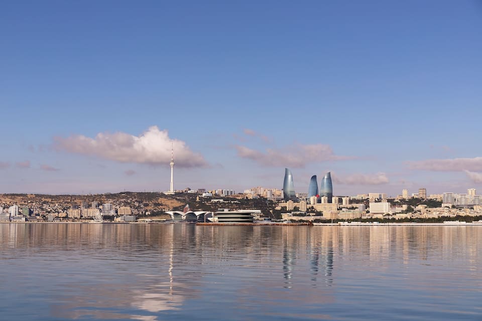 Silhueta urbana com edifícios modernos, uma torre e um corpo d'água refletindo a cidade.