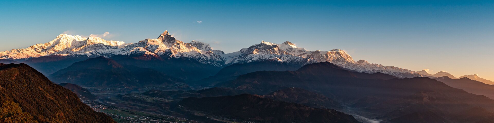 Uma cordilheira com picos nevados, um vale com uma cidade e um céu claro.