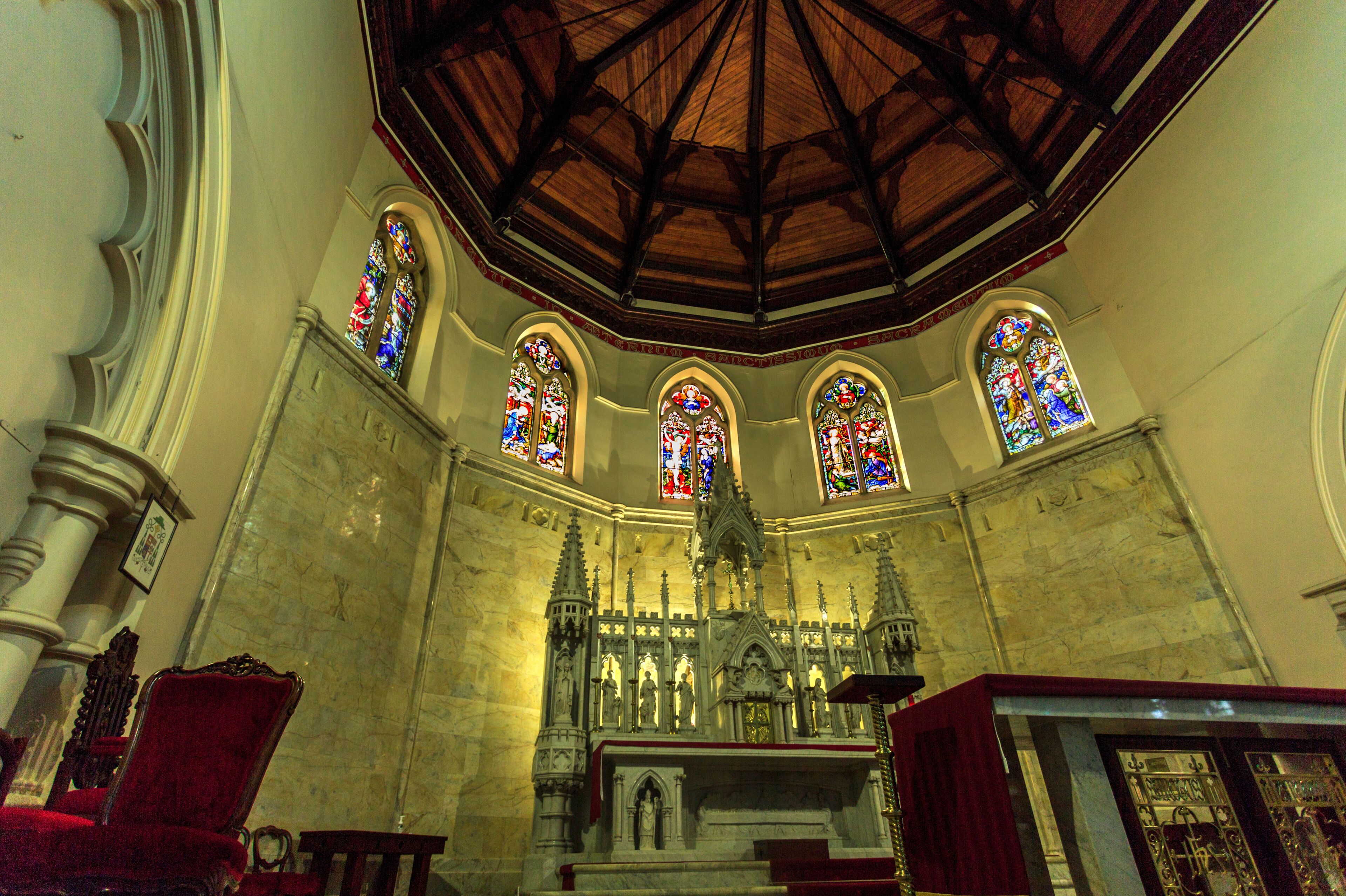 Interior de igreja com vitrais, teto de madeira e altar central.