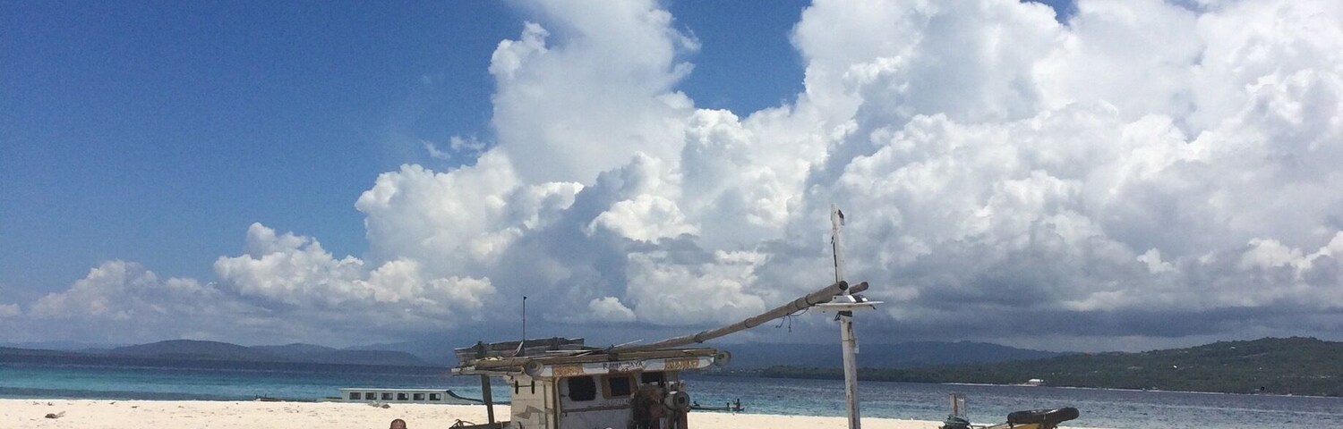 Um barco numa praia arenosa com céu azul límpido e montanhas ao longe.
