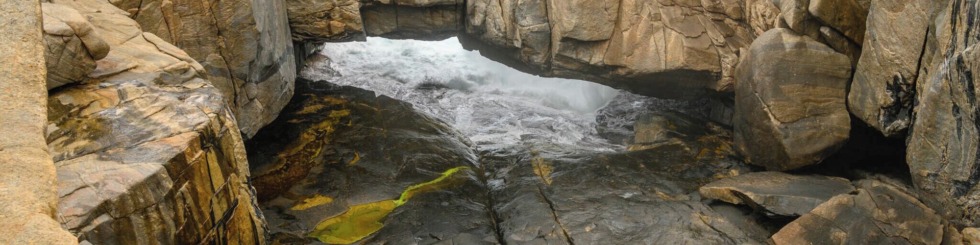 Paisagem costeira rochosa com um estreito canal entre grandes pedras.