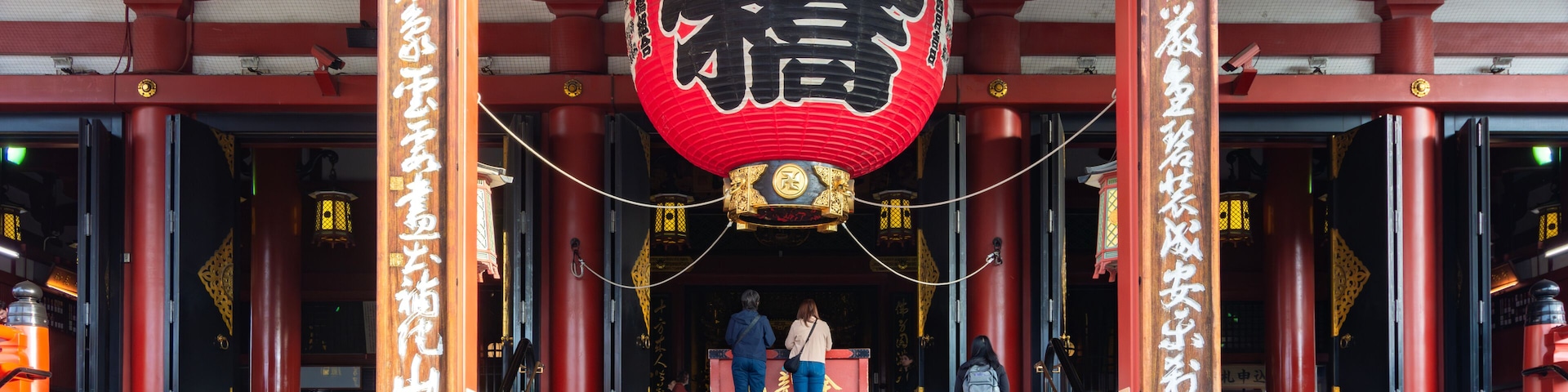 Entrada tradicional de um templo japonês, com portões torii vermelhos, um grande lança vermelha e degraus de pedra que levam ao salão principal.