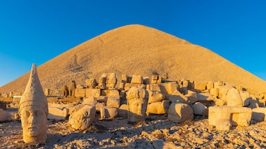 Ruínas antigas com grandes blocos de pedra e uma pirâmide ao fundo.