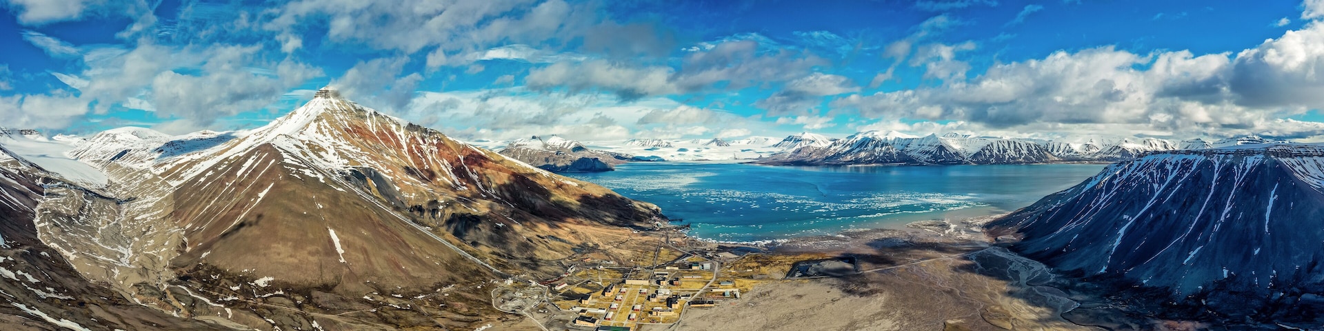 Paisagem montanhosa com uma cidade no vale, uma grande extensão de água e picos cobertos de neve.