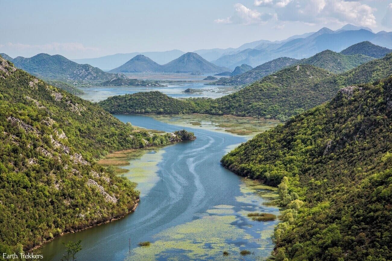 Um rio serpenteando por uma paisagem montanhosa, com vegetação densa e montanhas ao longe.