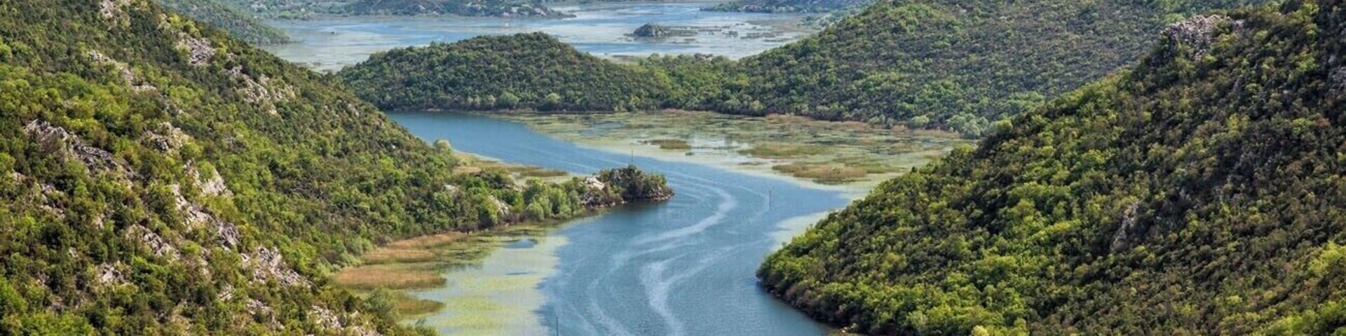 Um rio serpenteando por uma paisagem montanhosa, com vegetação densa e montanhas ao longe.