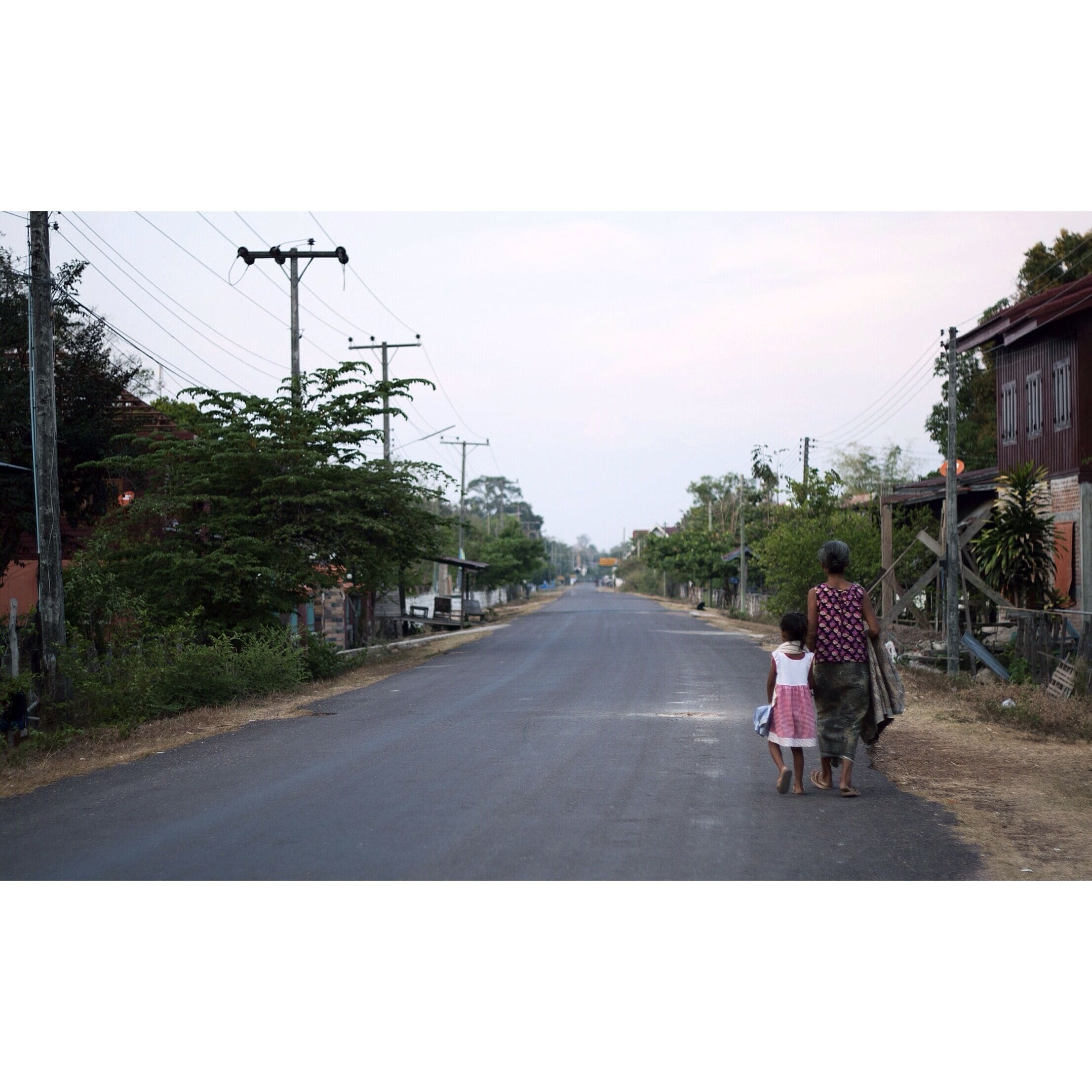 Uma estrada rural ladeada por postes de eletricidade e vegetação.