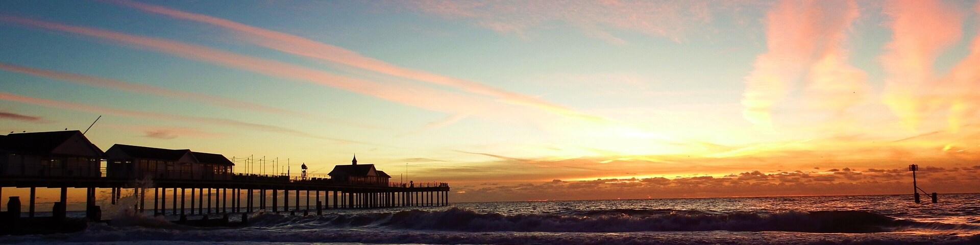 Um cais se estendendo para o oceano ao pôr do sol, com ondas quebrando na costa.