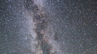 Céu noturno repleto de estrelas e da Via Láctea, com iurtes em primeiro plano.
