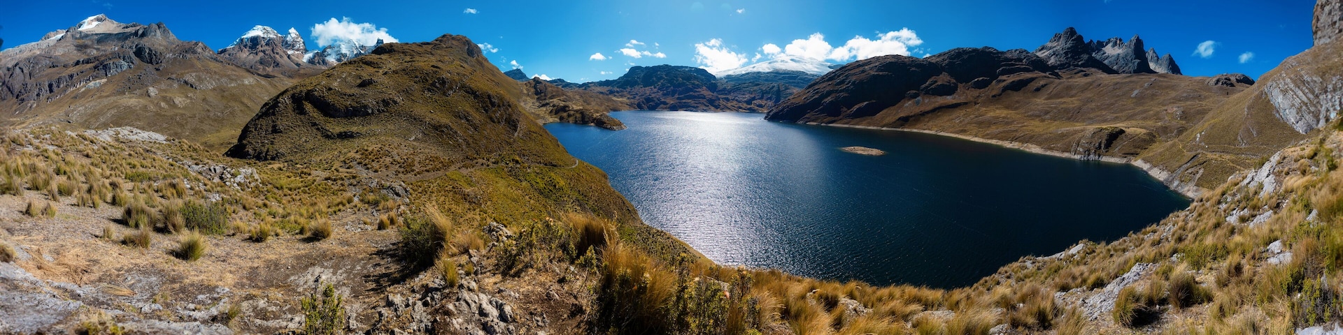 Paisagem montanhosa com um lago rodeado por terreno rochoso e vegetação esparsa.