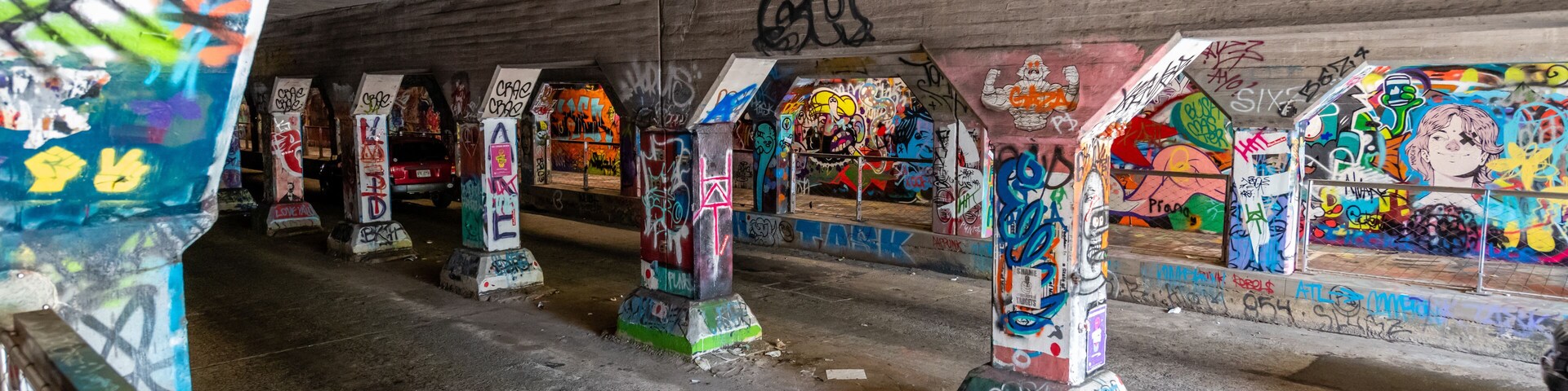 Uma passagem subterrânea com grafites coloridos nas paredes e pilares.