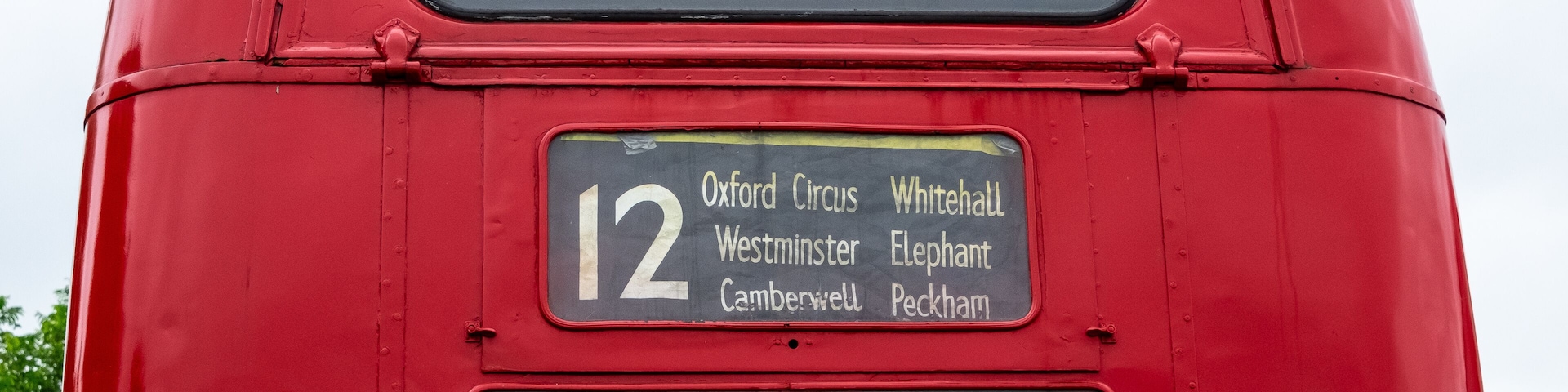 Parte traseira de um ônibus de dois andares vermelho, com uma placa de destino indicando '12 Oxford Circus, Westminster, Elephant & Castle'.