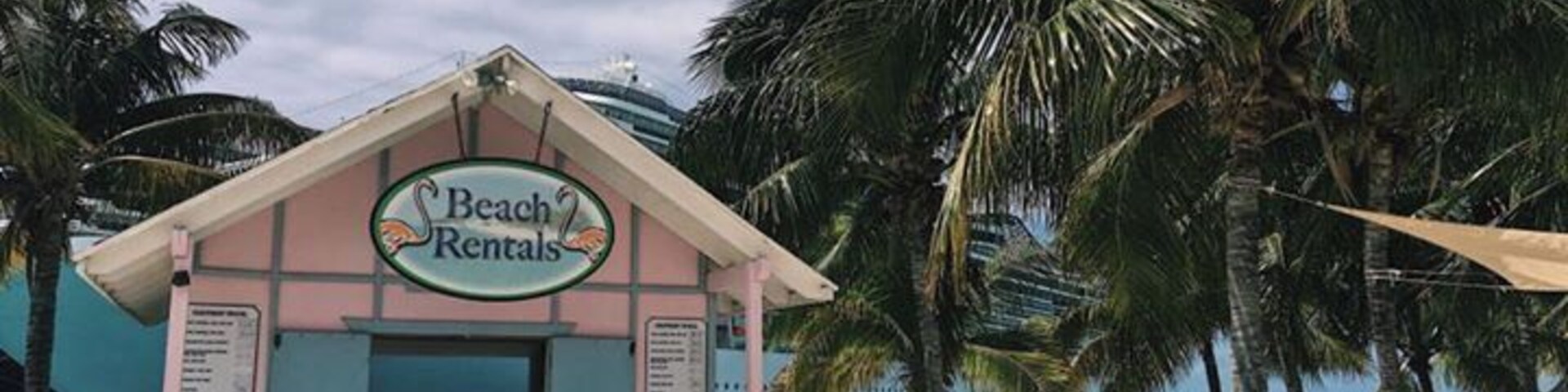 Quiosque de aluguel de praia com um letreiro, cercado por palmeiras e pessoas na praia.