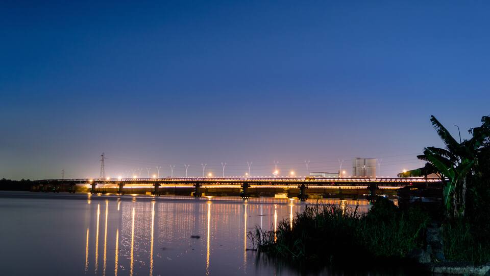 Uma ponte ao entardecer, com luzes refletindo na água.