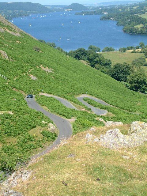 Uma estrada sinuosa por uma paisagem verde com um lago ao fundo.