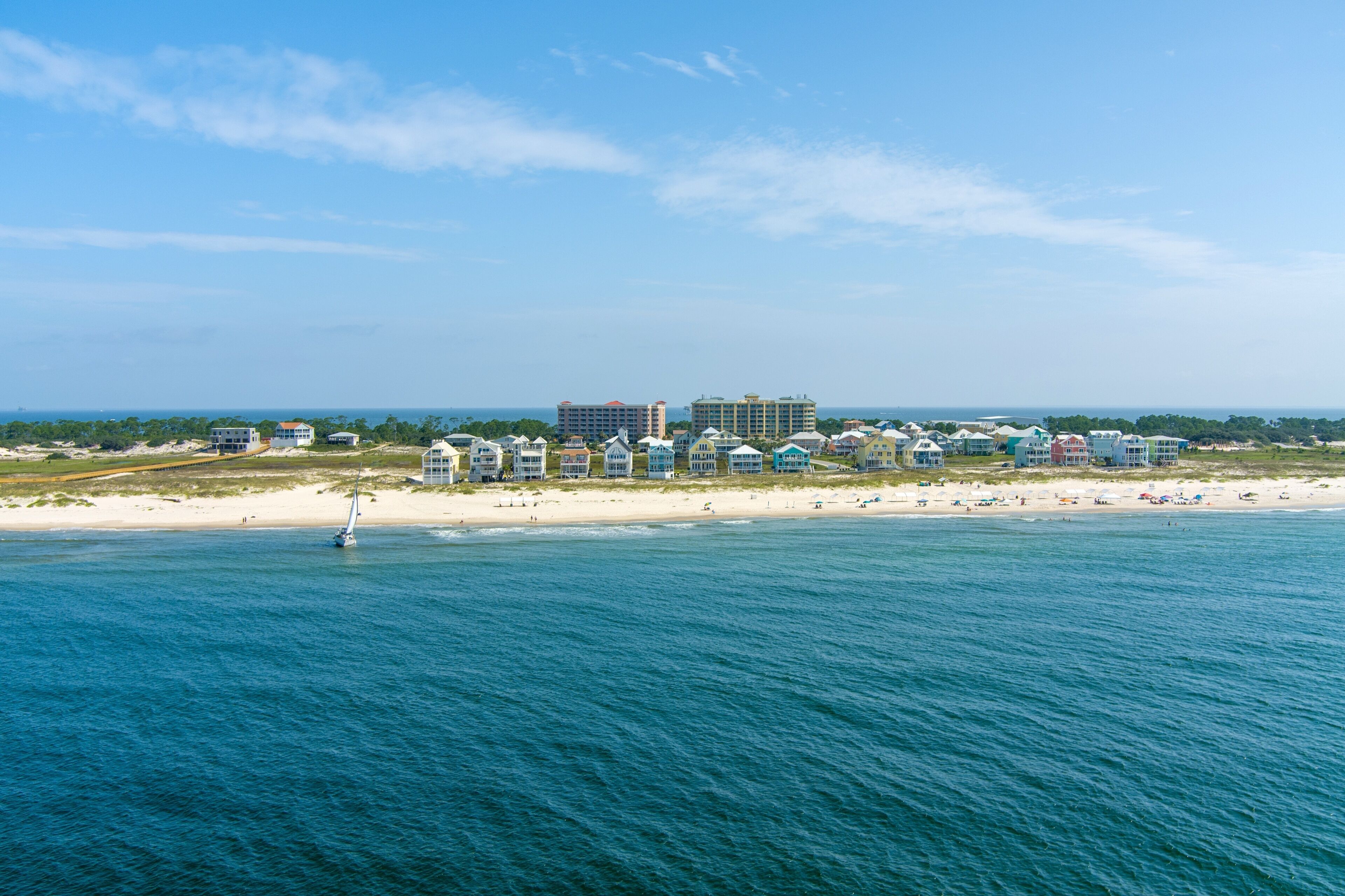Um resort costeiro com villas na praia, uma praia de areia e um veleiro na água.