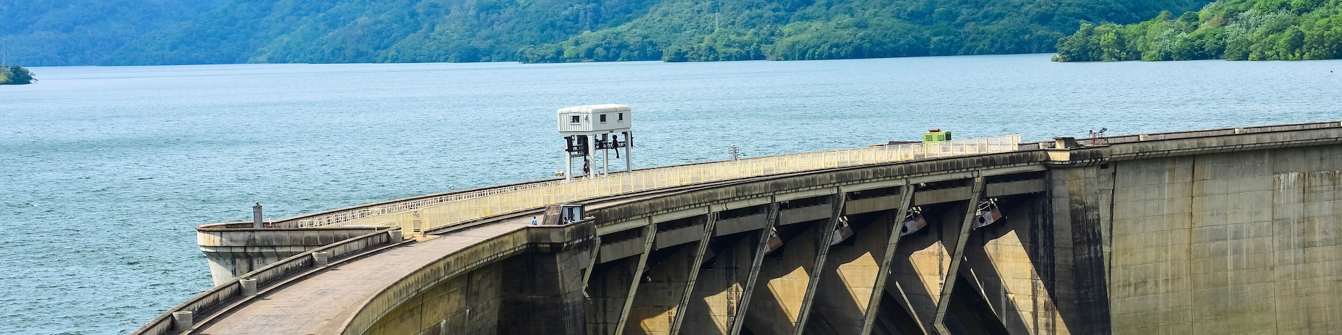 Uma barragem com uma torre de controle, emoldurada por uma paisagem montanhosa e um lago tranquilo.
