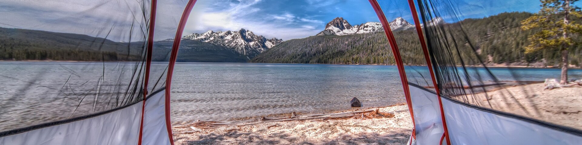Uma tenda com vista para um lago, montanhas e uma floresta.