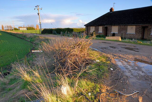 Uma estrada rural com poças, um edifício e um campo gramado.