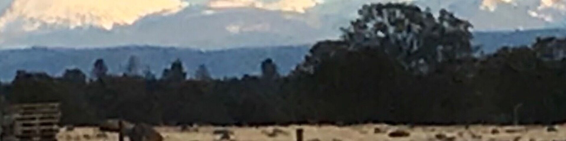 Paisagem rural com uma pilha de fardos de feno, uma cerca e uma cadeia de montanhas ao fundo.