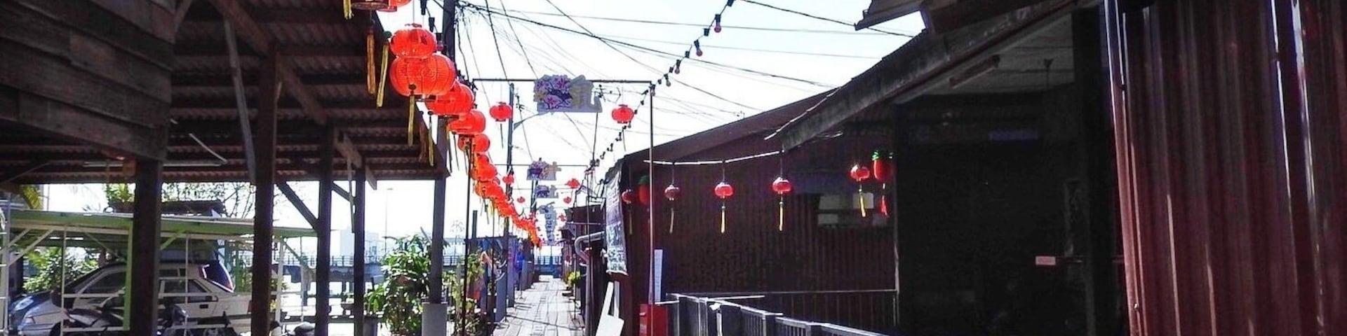 Uma passarela de madeira com lanternas vermelhas penduradas, cercada por edifícios e motocicletas estacionadas.