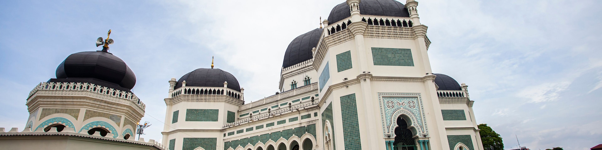 Uma grande mesquita com duas cúpulas e um minarete, rodeada por um pátio.