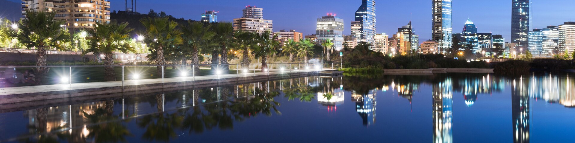 Horizonte urbano ao entardecer, com edifícios refletidos em águas calmas.
