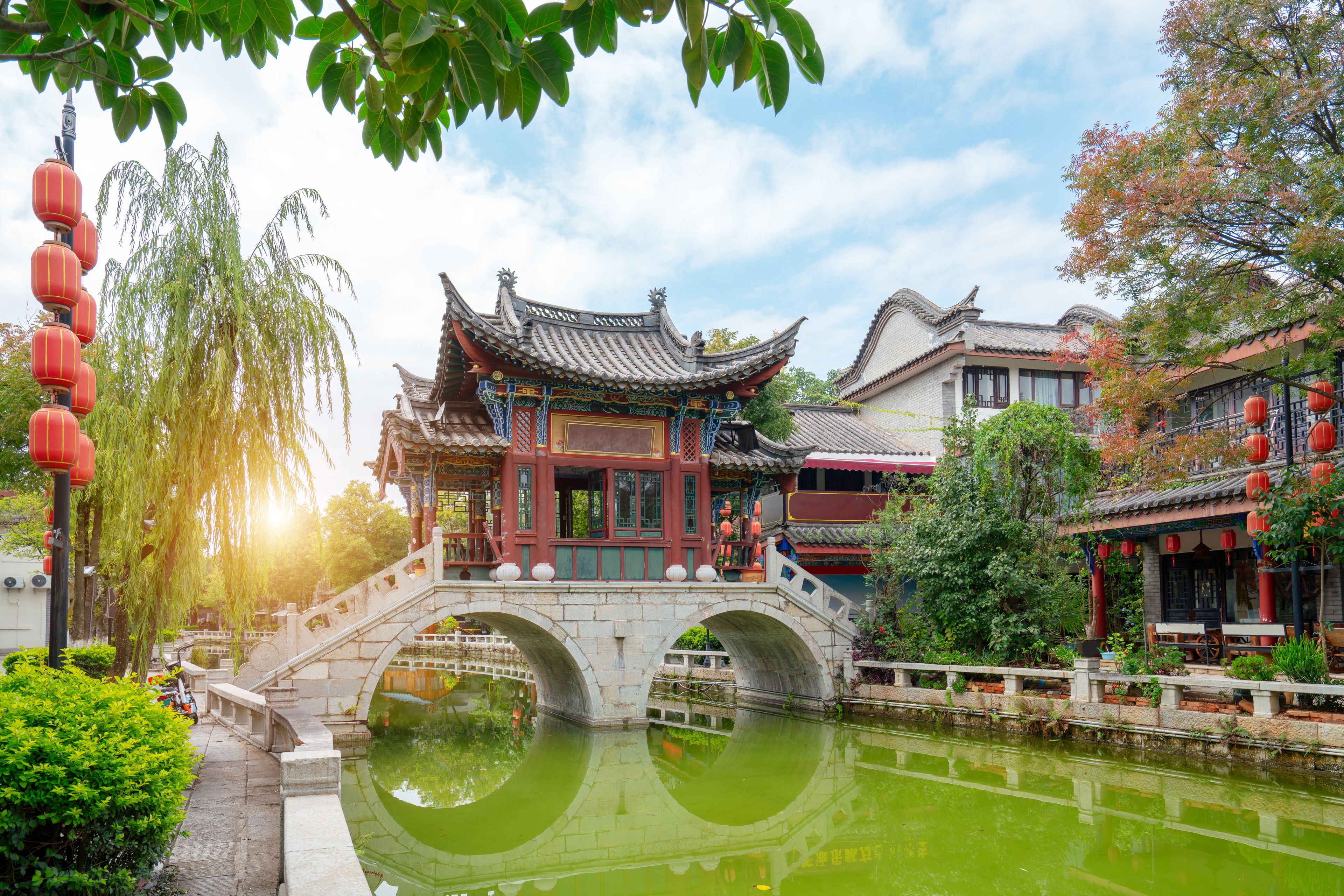 Um pavilhão tradicional chinês com arquitetura elaborada, uma ponte de pedra e um lago.