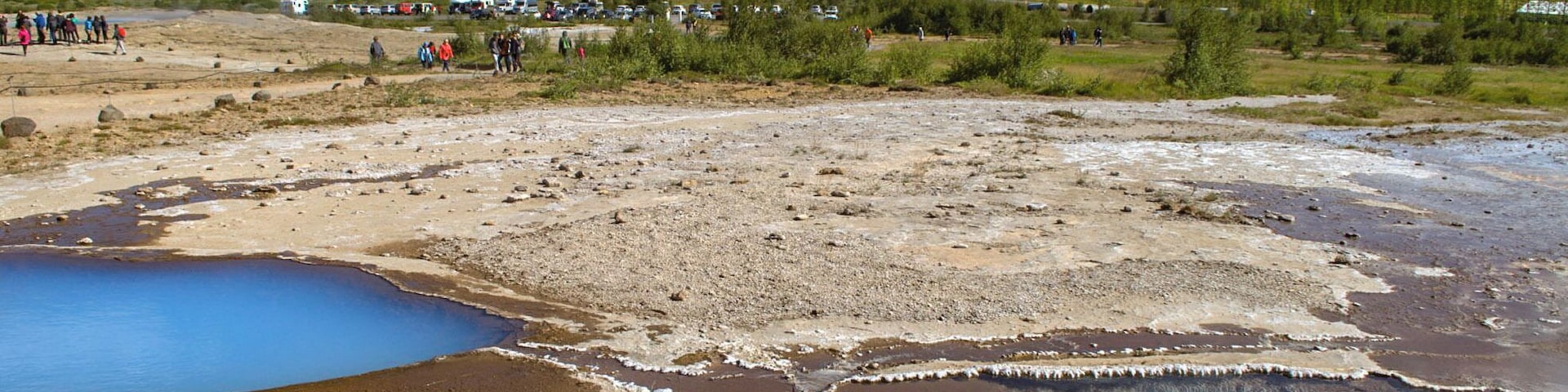 Uma área geotérmica com nascentes termais, um pequeno lago e um povoado distante.