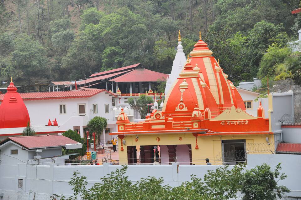 Um templo com cúpulas vermelhas e brancas, rodeado por vegetação e outros edifícios.