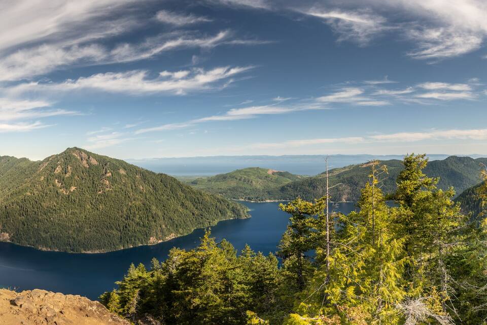 Paisagem montanhosa com um lago rodeado por florestas densas e um céu limpo.