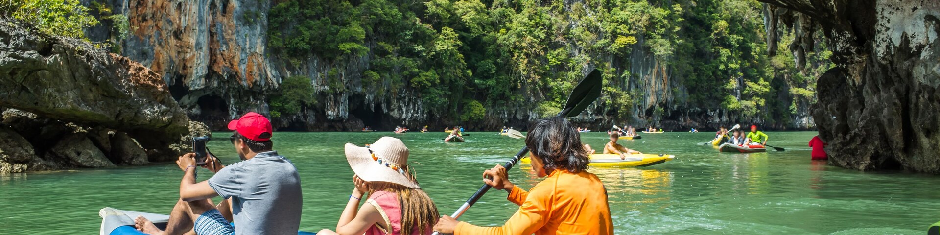 Pessoas em uma jangada azul em um rio calmo, rodeadas por penhascos rochosos e vegetação exuberante.