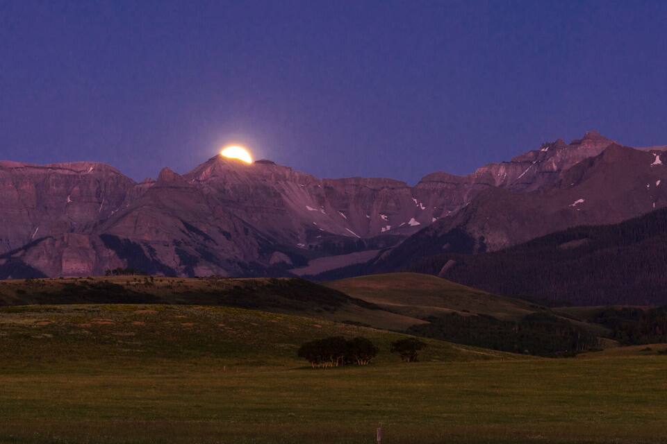 Uma cordilheira com um pico proeminente sob a lua cheia.