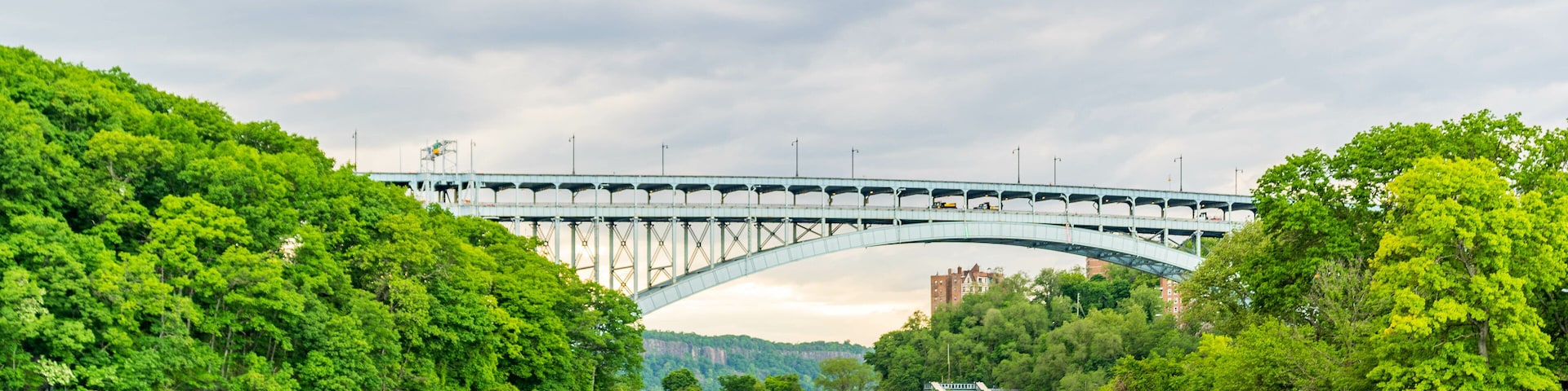 Uma ponte verde sobre um rio calmo, rodeada por vegetação exuberante e árvores.