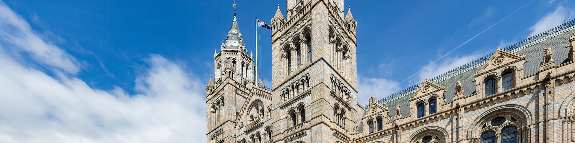 Um edifício histórico imponente com duas torres destacadas, uma grande entrada em arco e uma praça ampla.