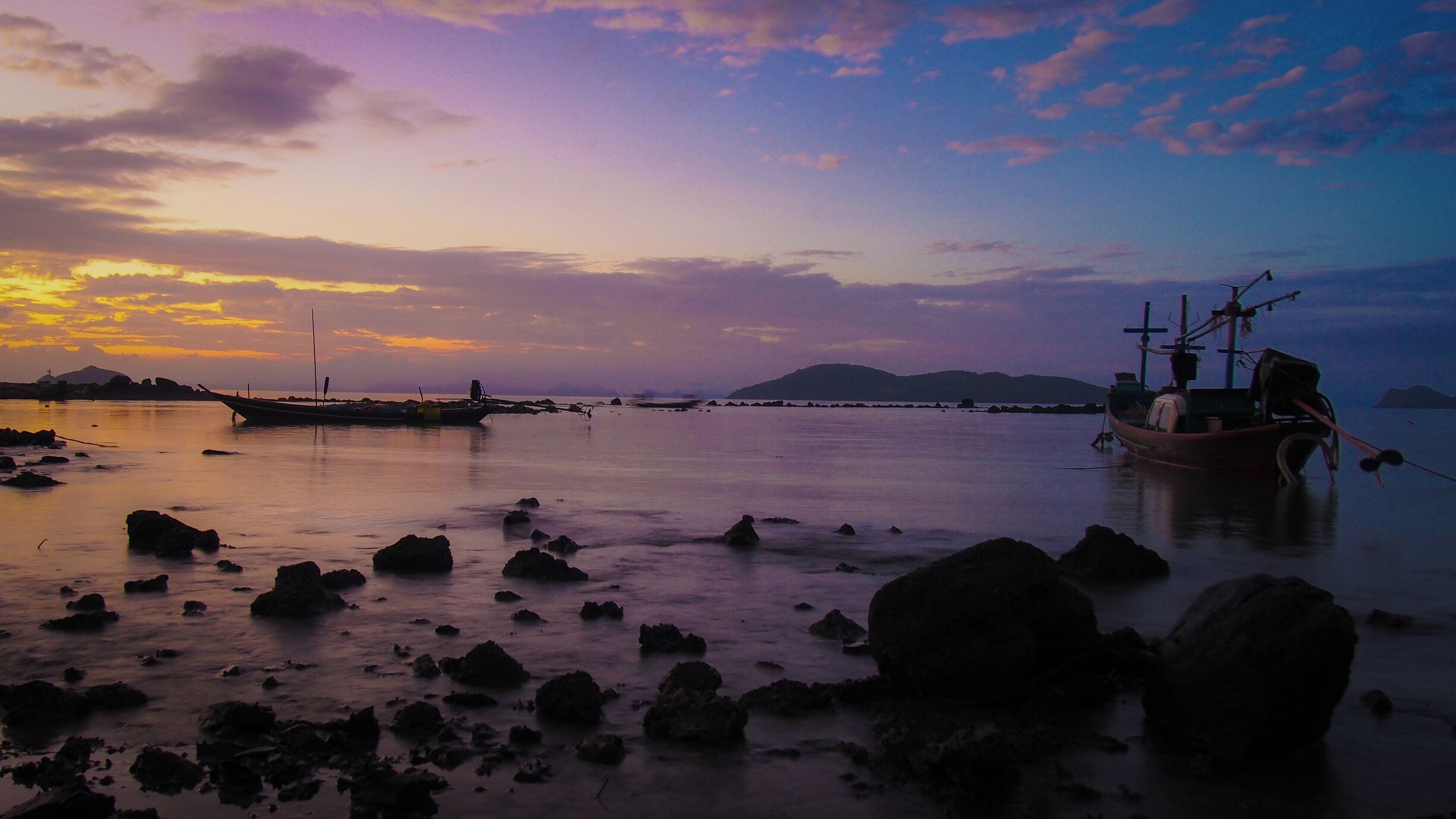 Cena costeira tranquila com barcos ancorados perto de rochas ao pôr do sol.